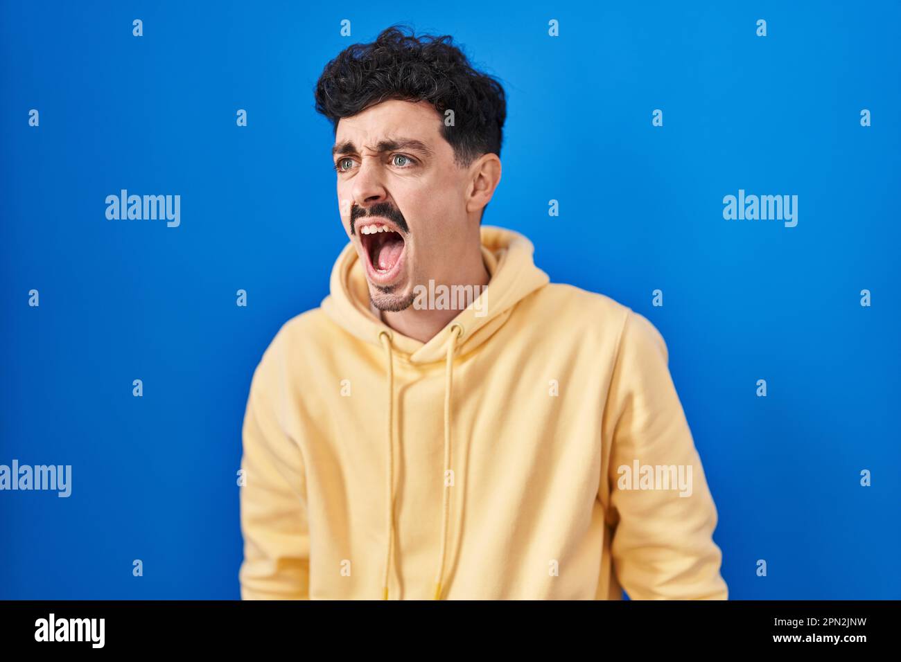 Hispanic man standing over blue background angry and mad screaming ...