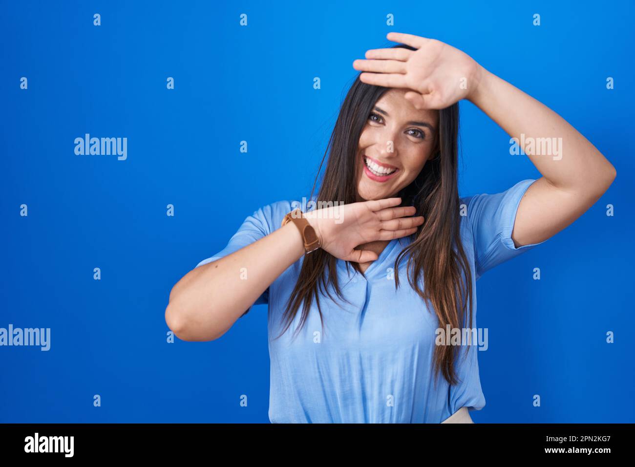 Young brunette woman standing over blue background smiling cheerful ...