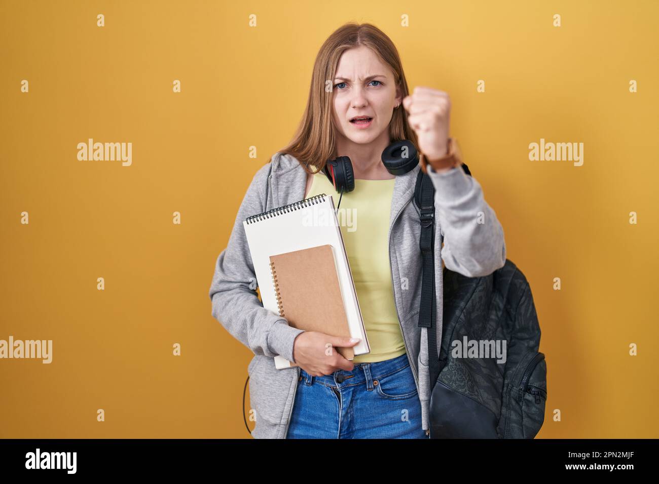 Young caucasian woman wearing student backpack and holding books angry ...