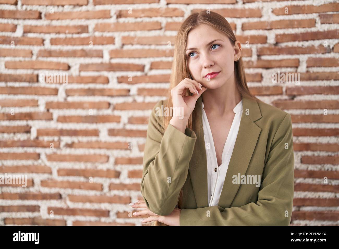 Young caucasian woman standing over bricks wall background with hand on ...