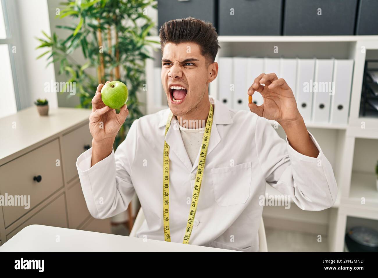 Young hispanic doctor man holding pills for fat loss angry and mad ...