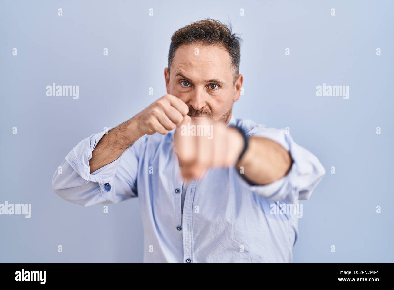 Middle age caucasian man standing over blue background punching fist to ...