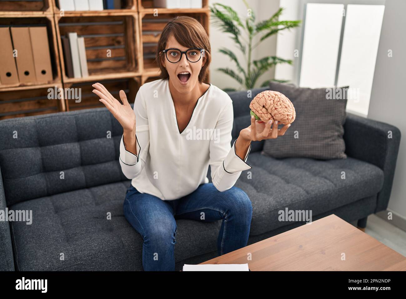 Brunette woman working at therapy office holding brain celebrating ...