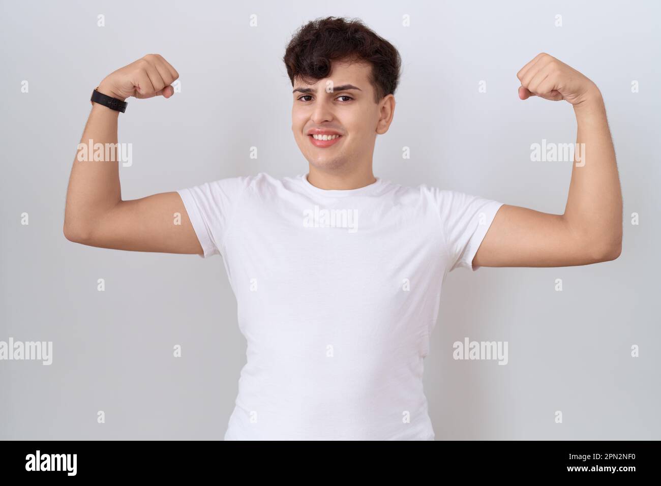 Young non binary man wearing casual white t shirt showing arms muscles ...