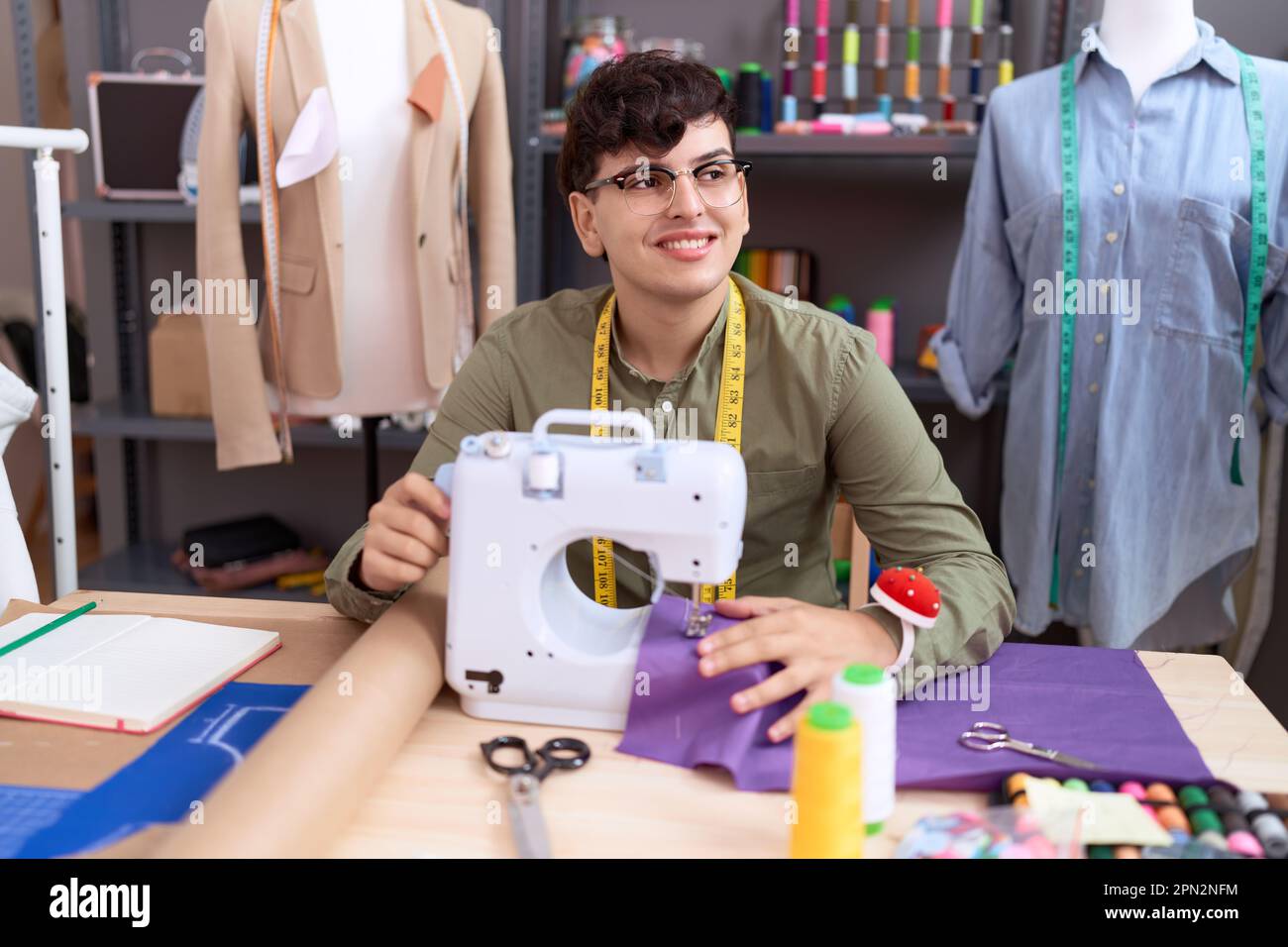 Non binary man tailor smiling confident using sewing machine at atelier ...