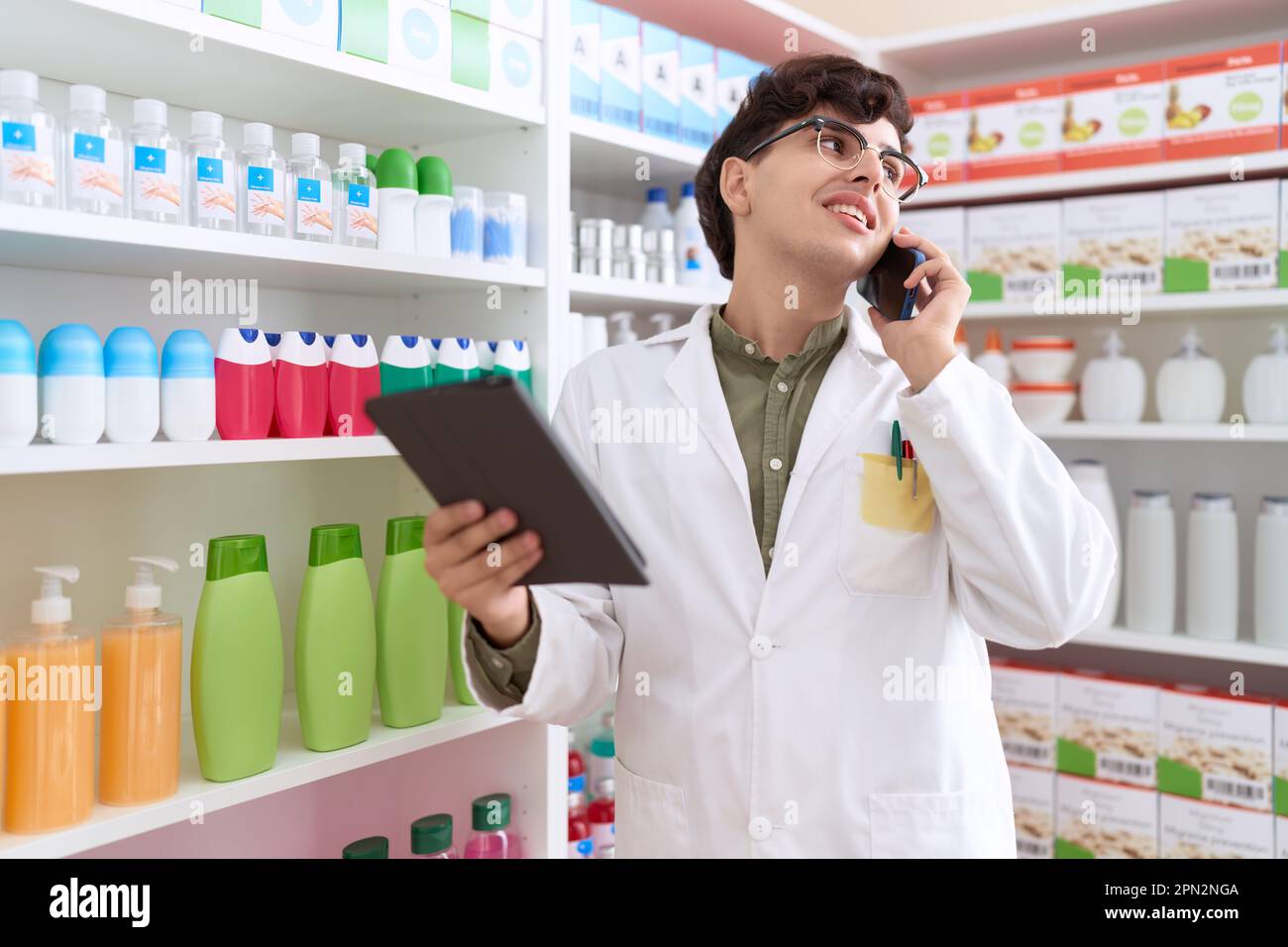 Non binary man pharmacist using touchpad talking on smartphone at ...