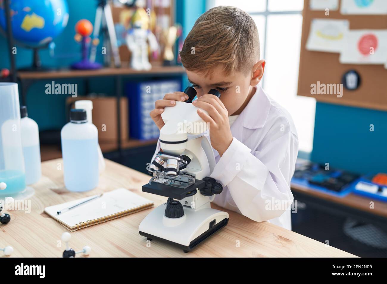 Adorable hispanic boy student using microscope at laboratory classroom ...