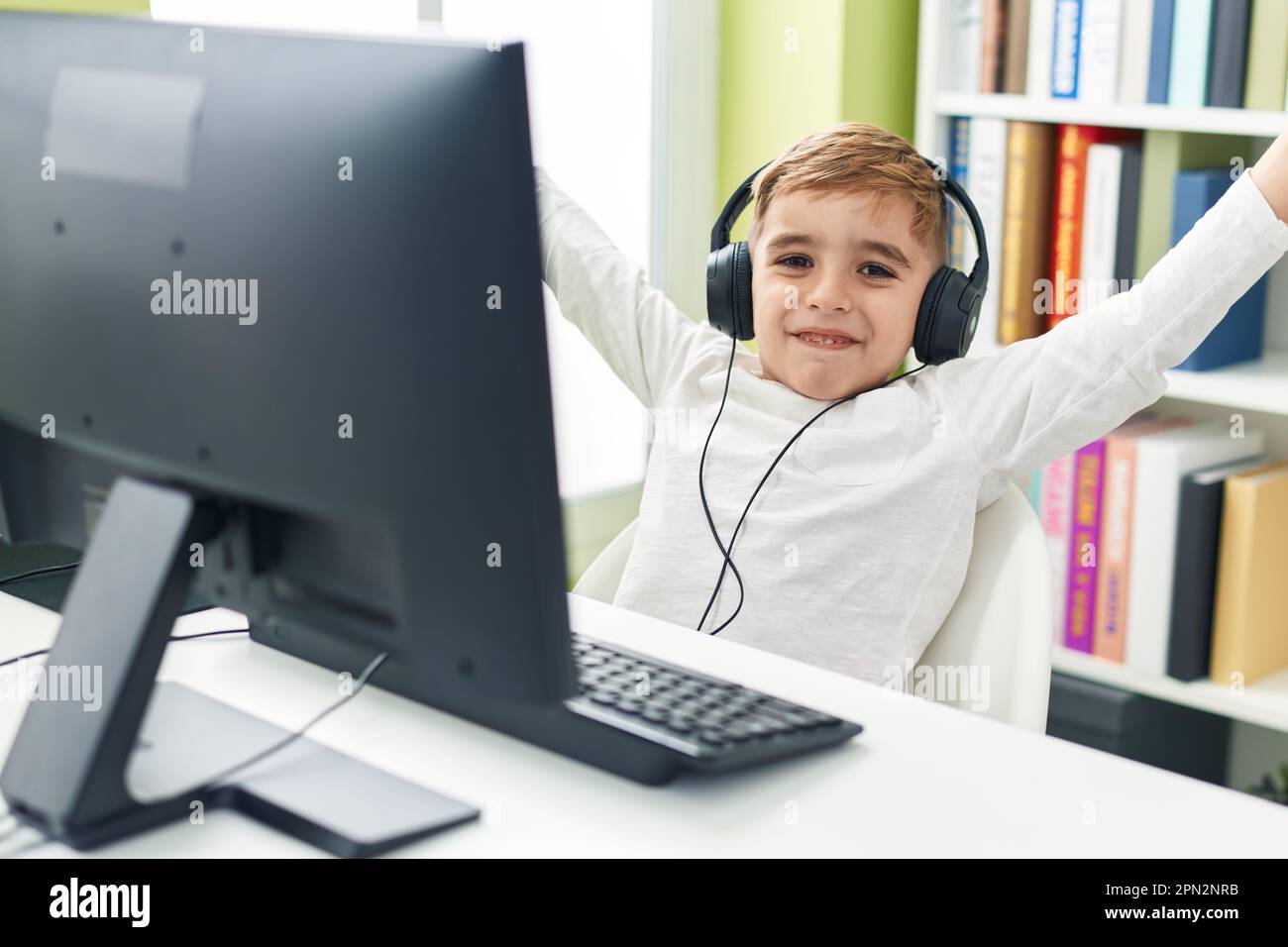 Adorable hispanic boy student using computer and headphones with winner ...