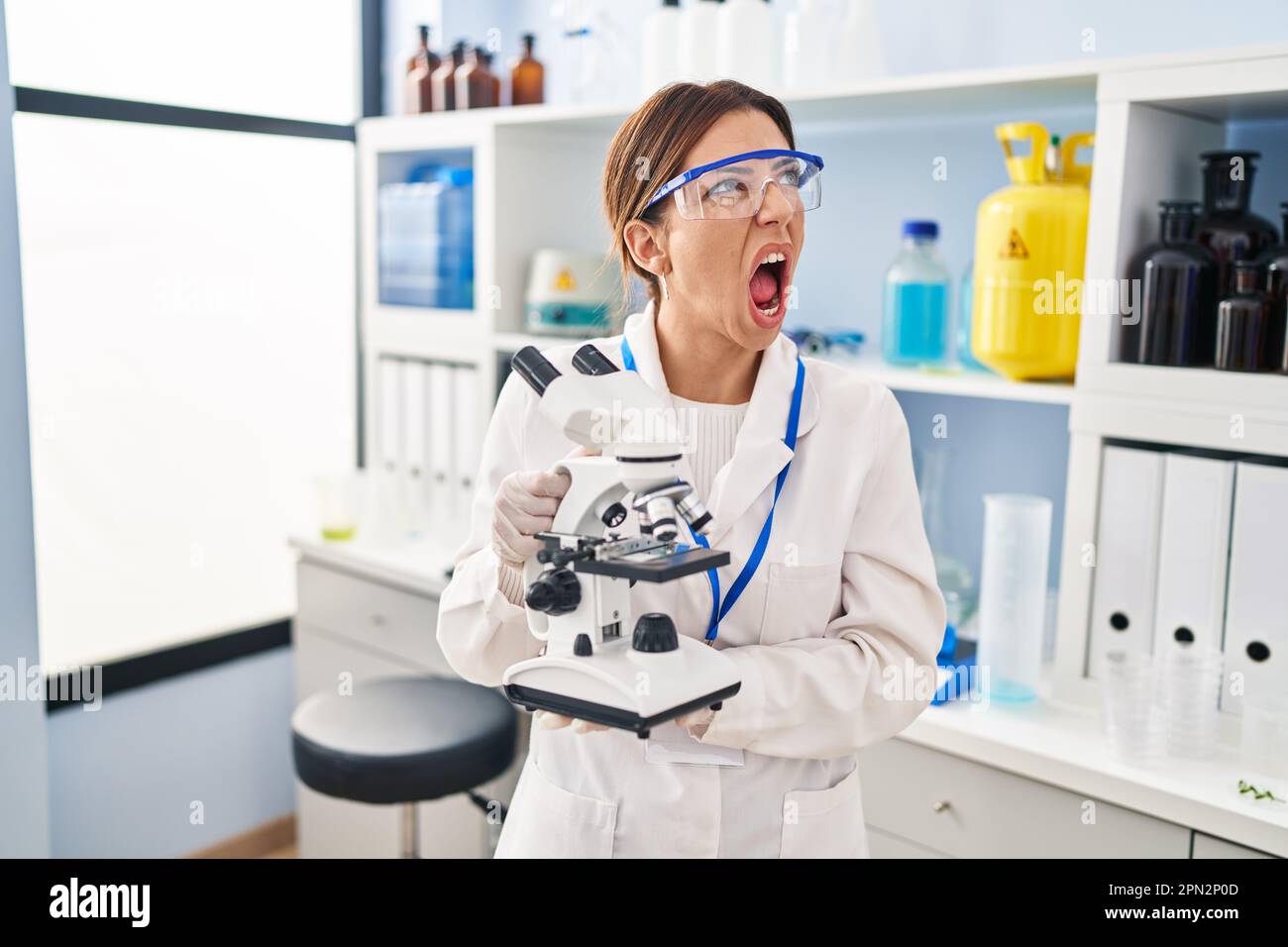 Young brunette woman working at scientist laboratory with microscope ...