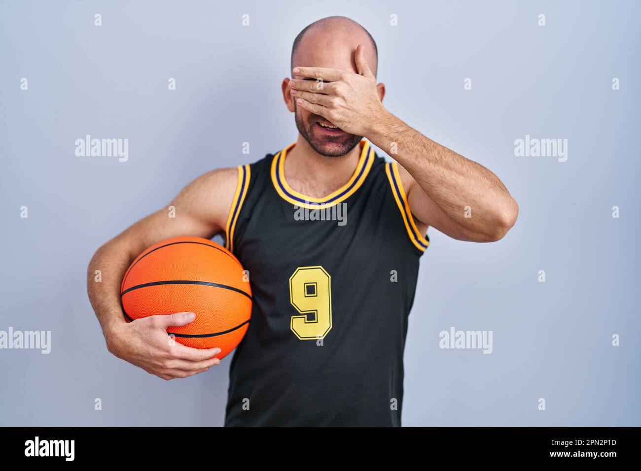 Young bald man with beard wearing basketball uniform holding ball ...