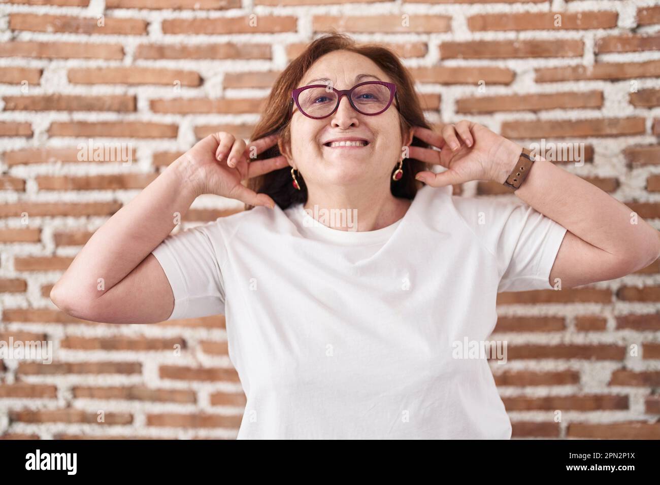 Senior woman with glasses standing over bricks wall smiling pulling ...