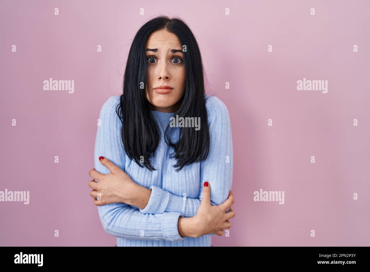 Hispanic woman standing over pink background shaking and freezing for ...