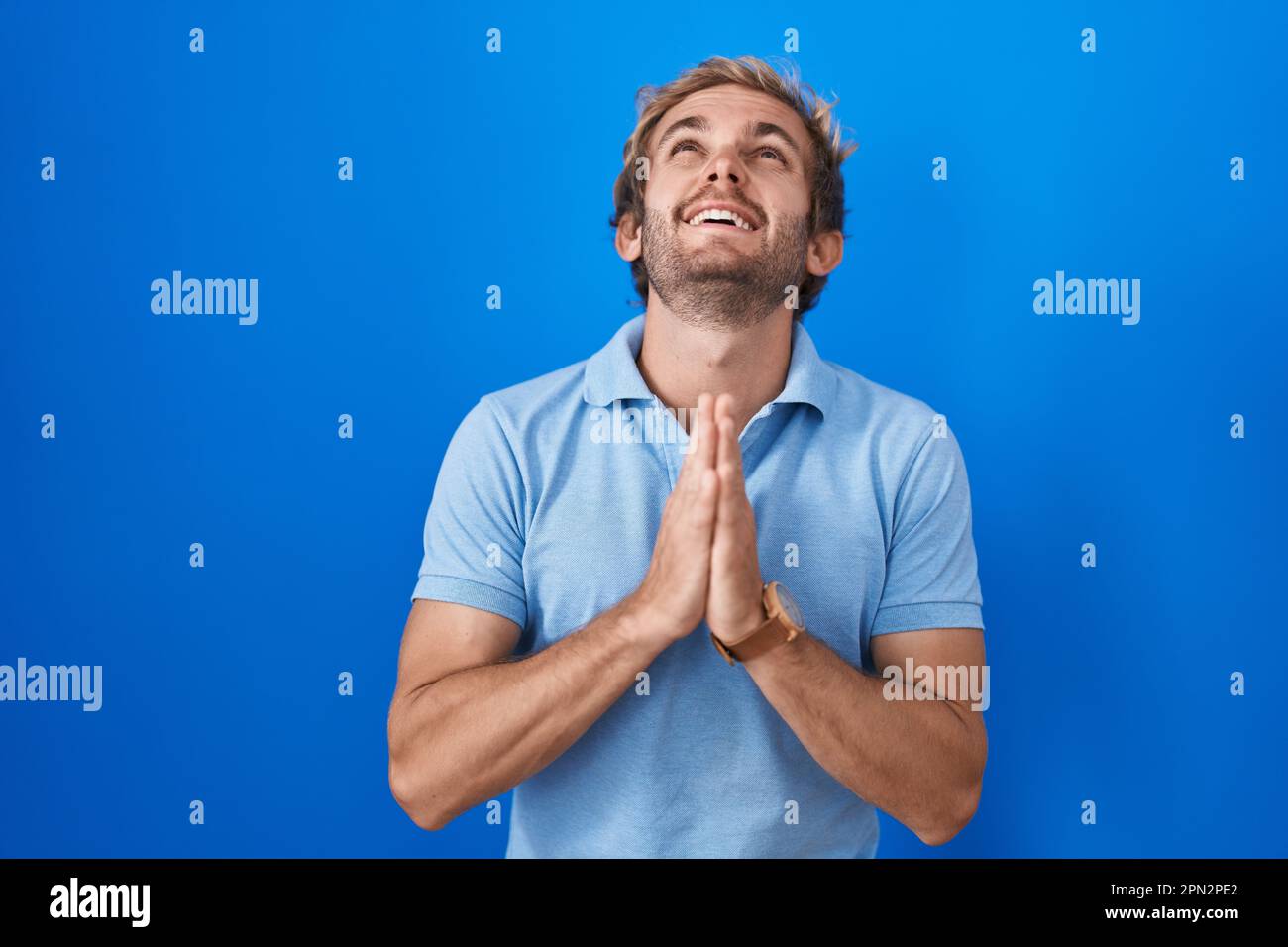Caucasian man standing over blue background begging and praying with ...