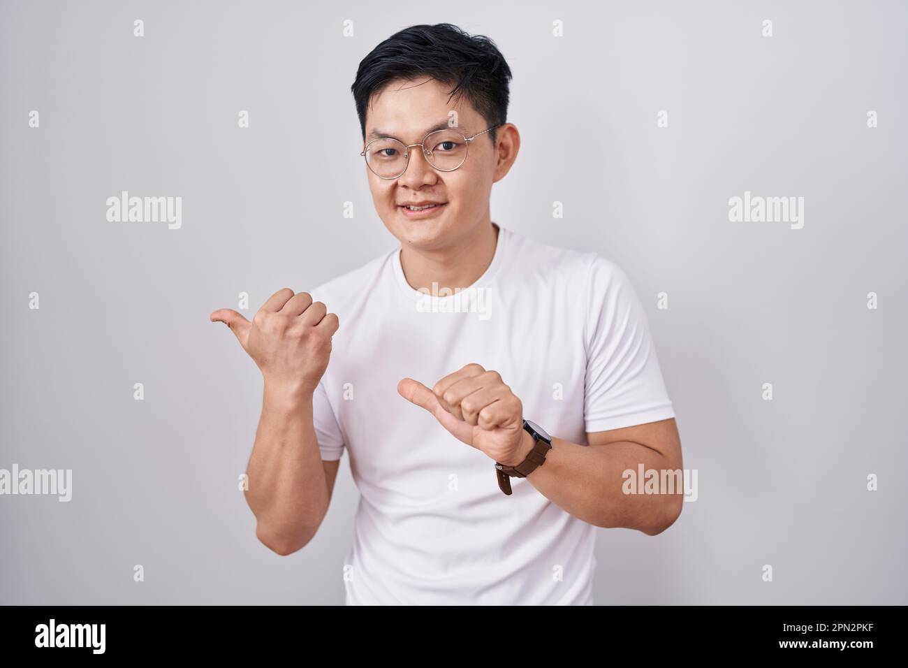 Young asian man standing over white background pointing to the back ...