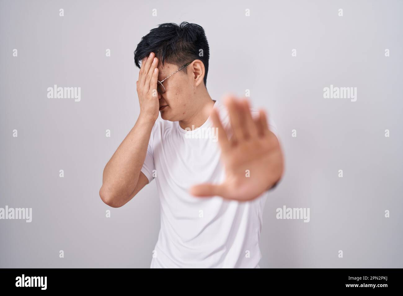 Young asian man standing over white background covering eyes with hands ...