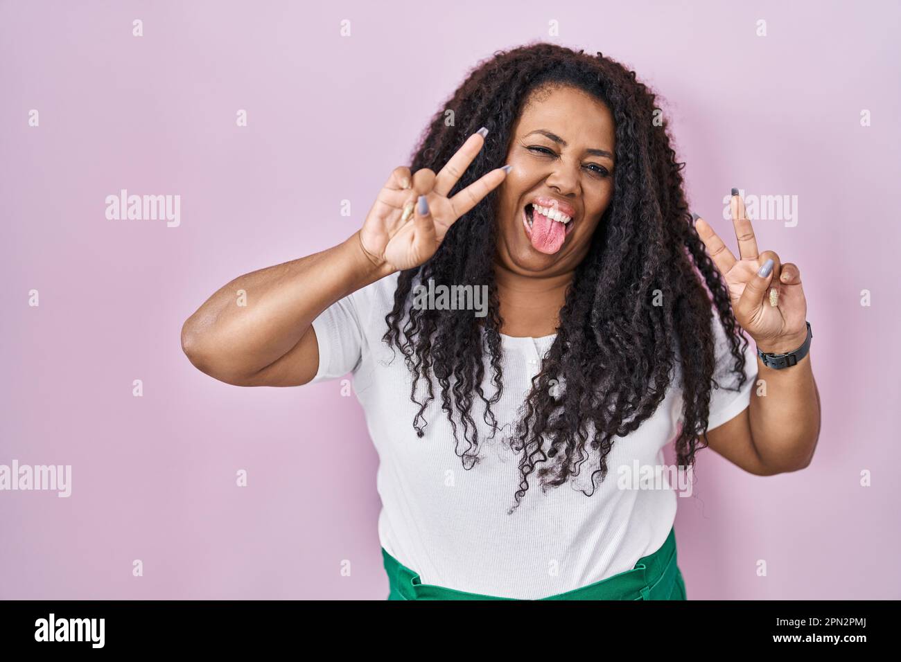 Plus size hispanic woman standing over pink background smiling with ...