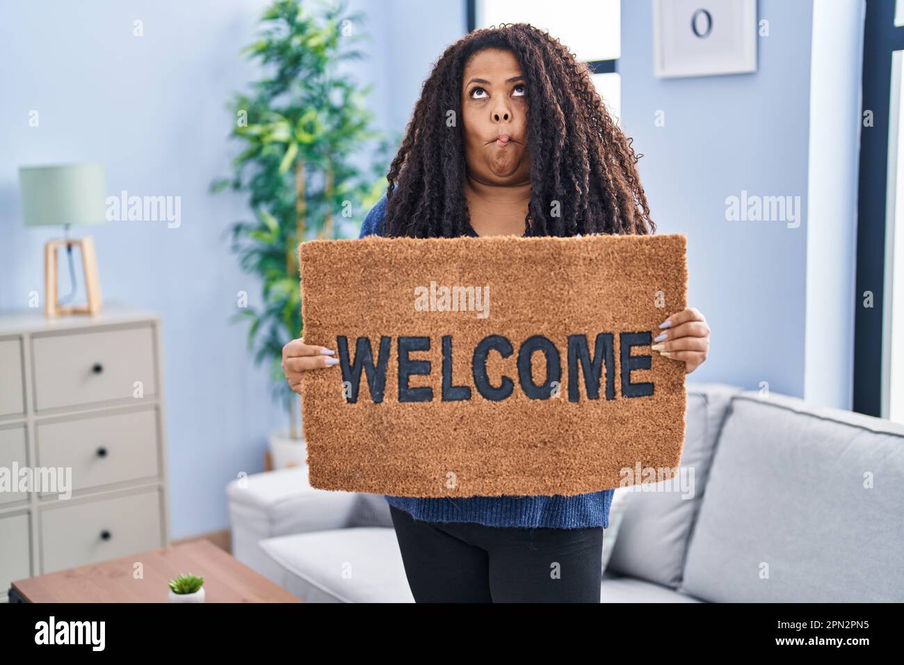 Plus size hispanic woman holding welcome doormat making fish face with ...