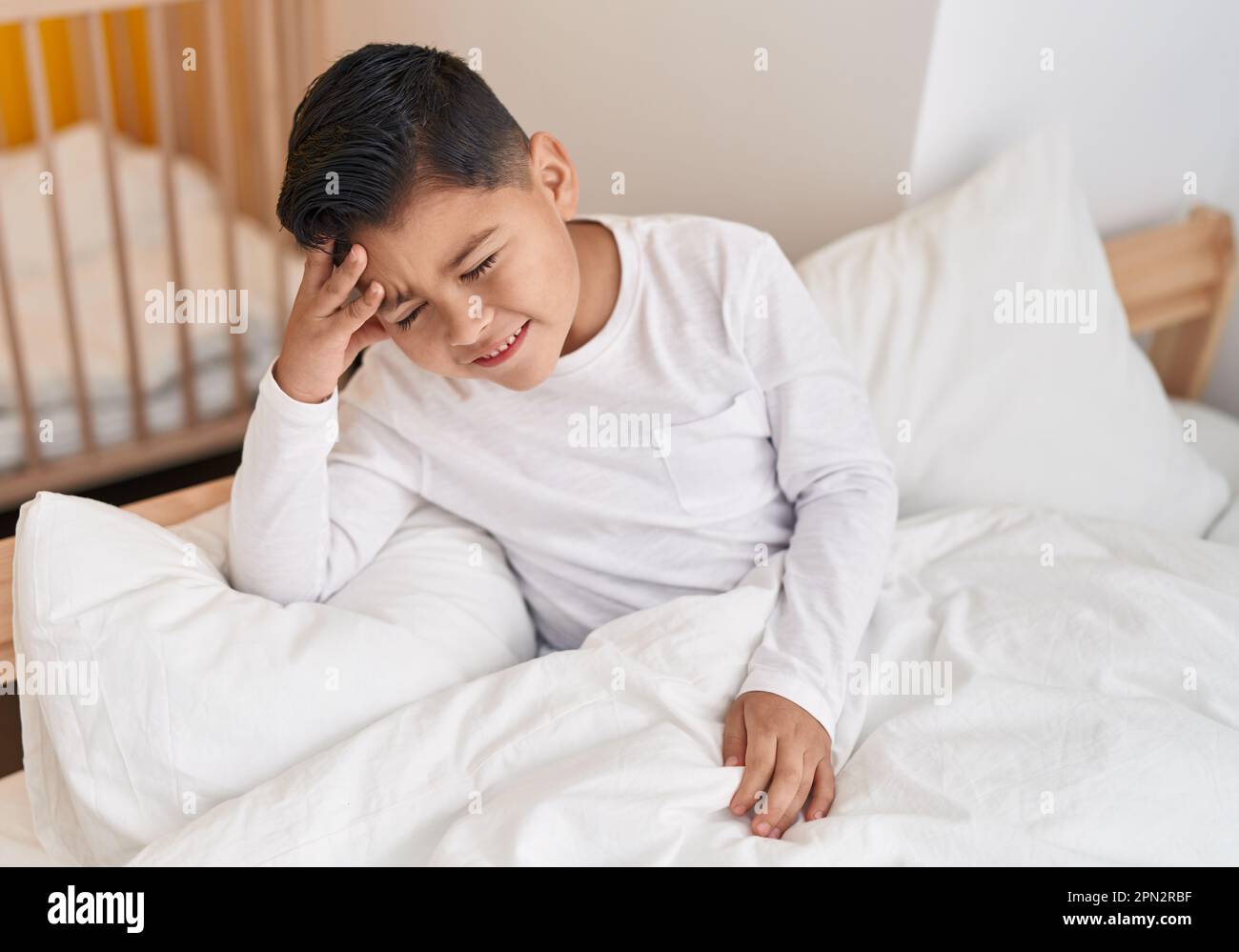 Adorable hispanic boy sitting on bed thinking at bedroom Stock Photo ...