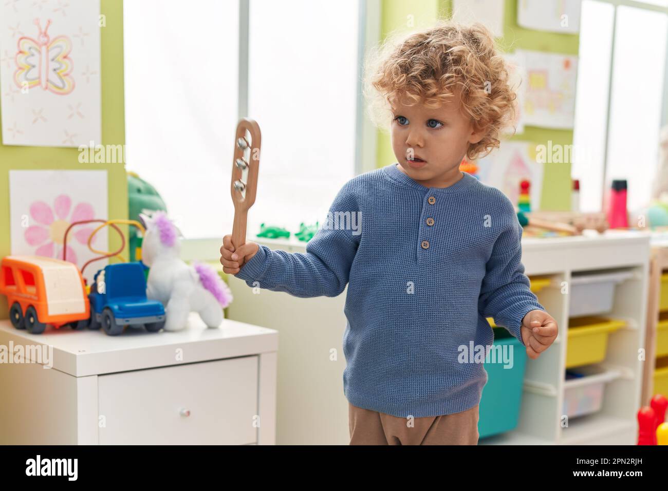 Adorable blond toddler standing with relaxed expression holding rattle ...