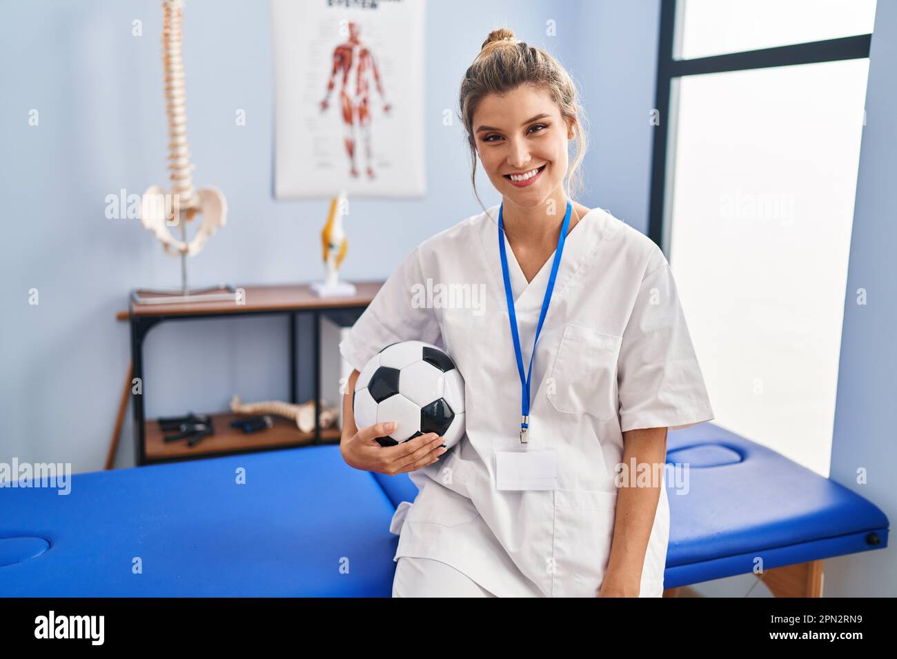 Young woman working at football therapy clinic looking positive and ...