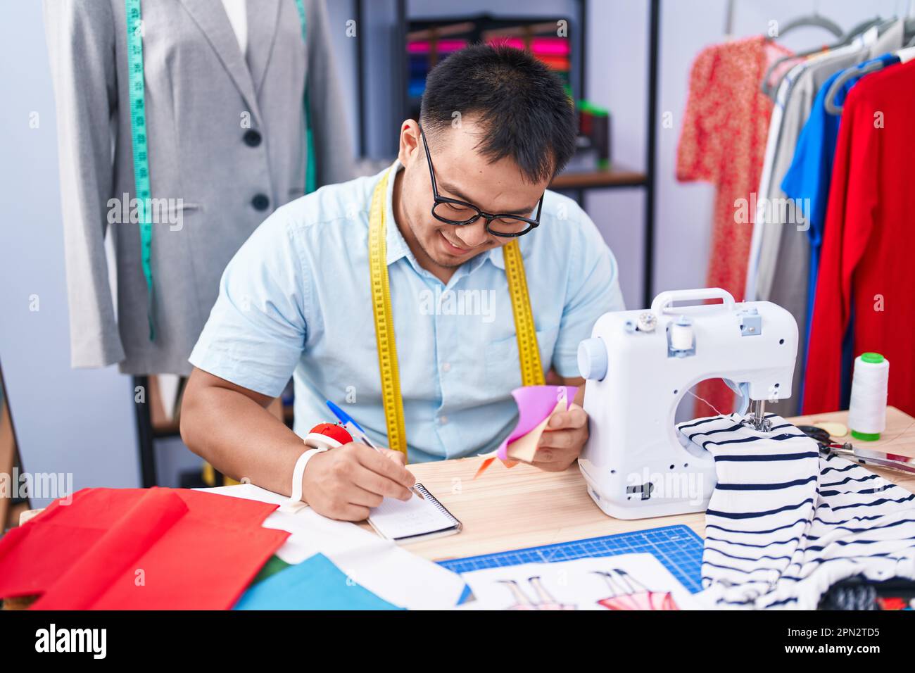 Young chinese man tailor writing on notebook holding cloth at tailor ...