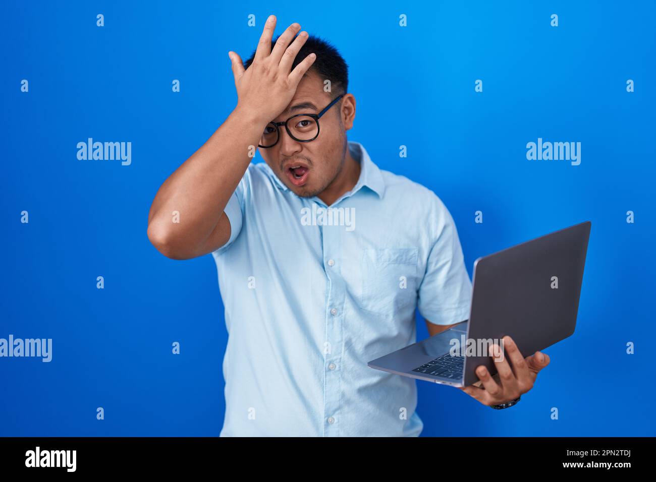 Chinese young man using computer laptop surprised with hand on head for ...