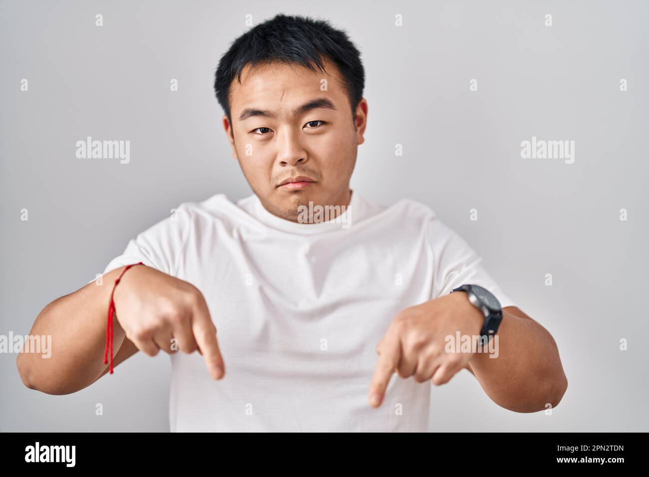 Young chinese man standing over white background pointing down looking ...