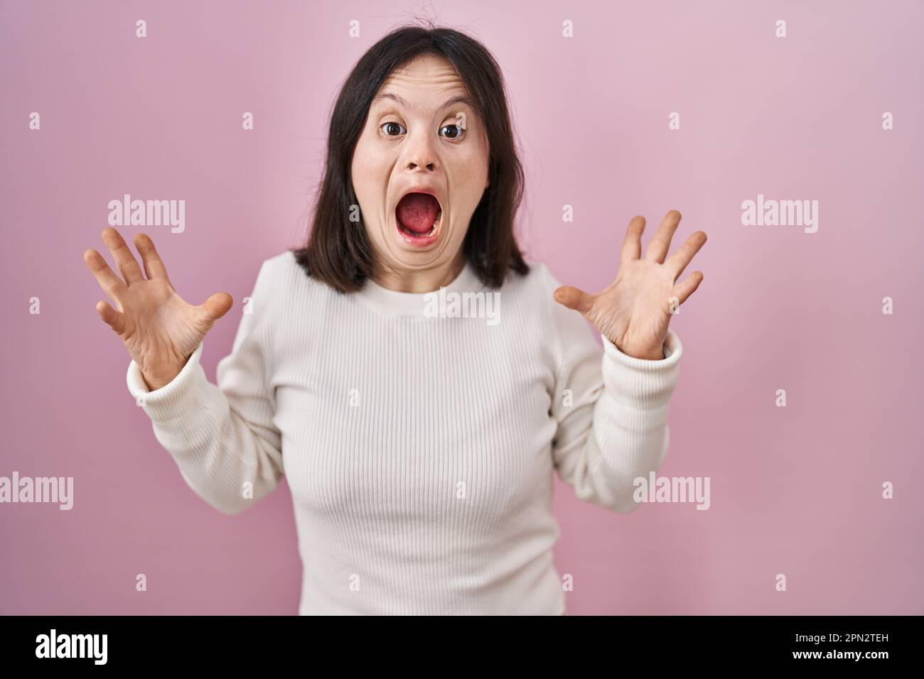 Woman with down syndrome standing over pink background celebrating ...