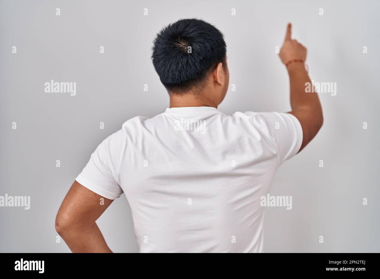 Young chinese man standing over white background posing backwards ...