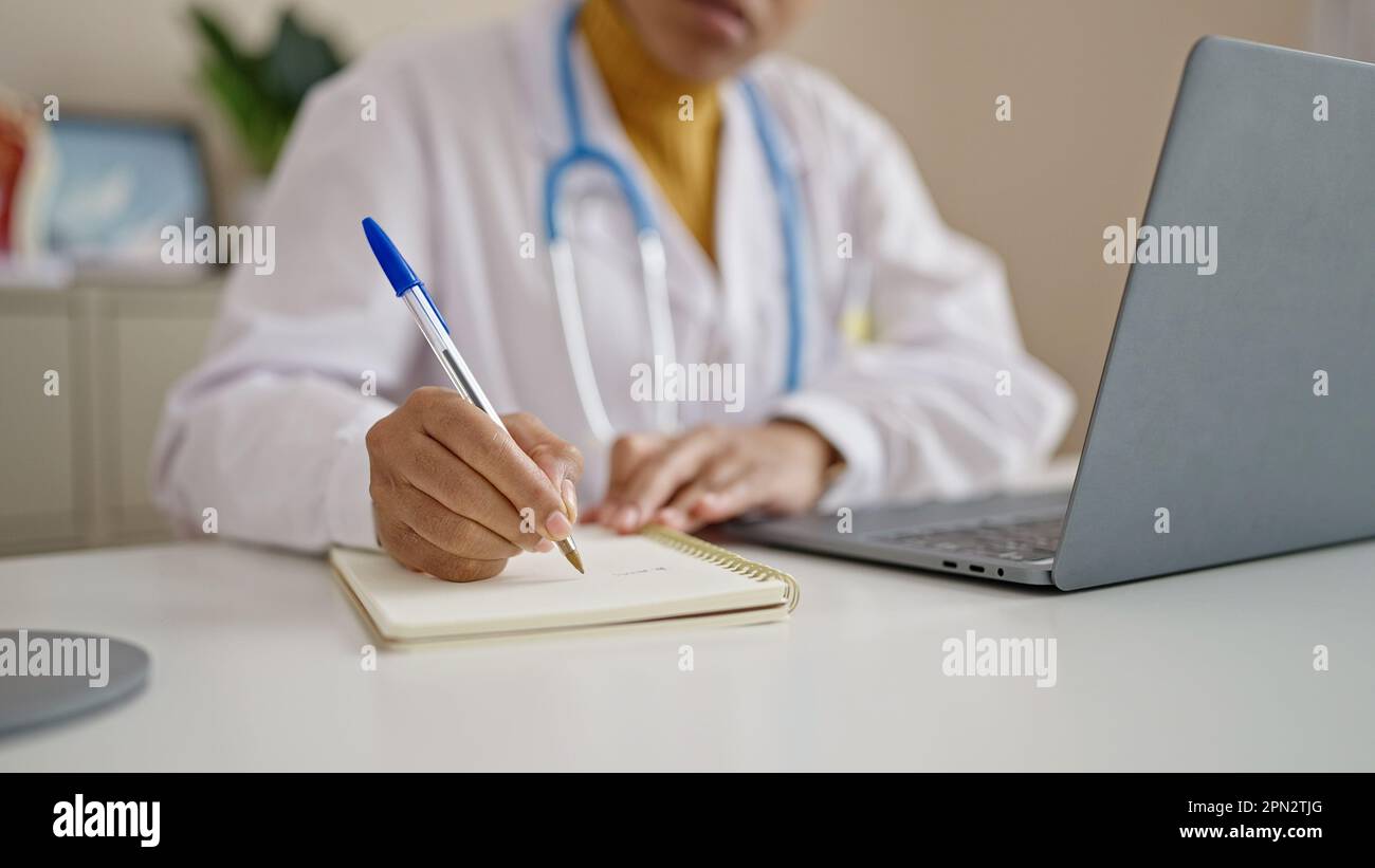 Young african american woman doctor using laptop taking notes at clinic ...