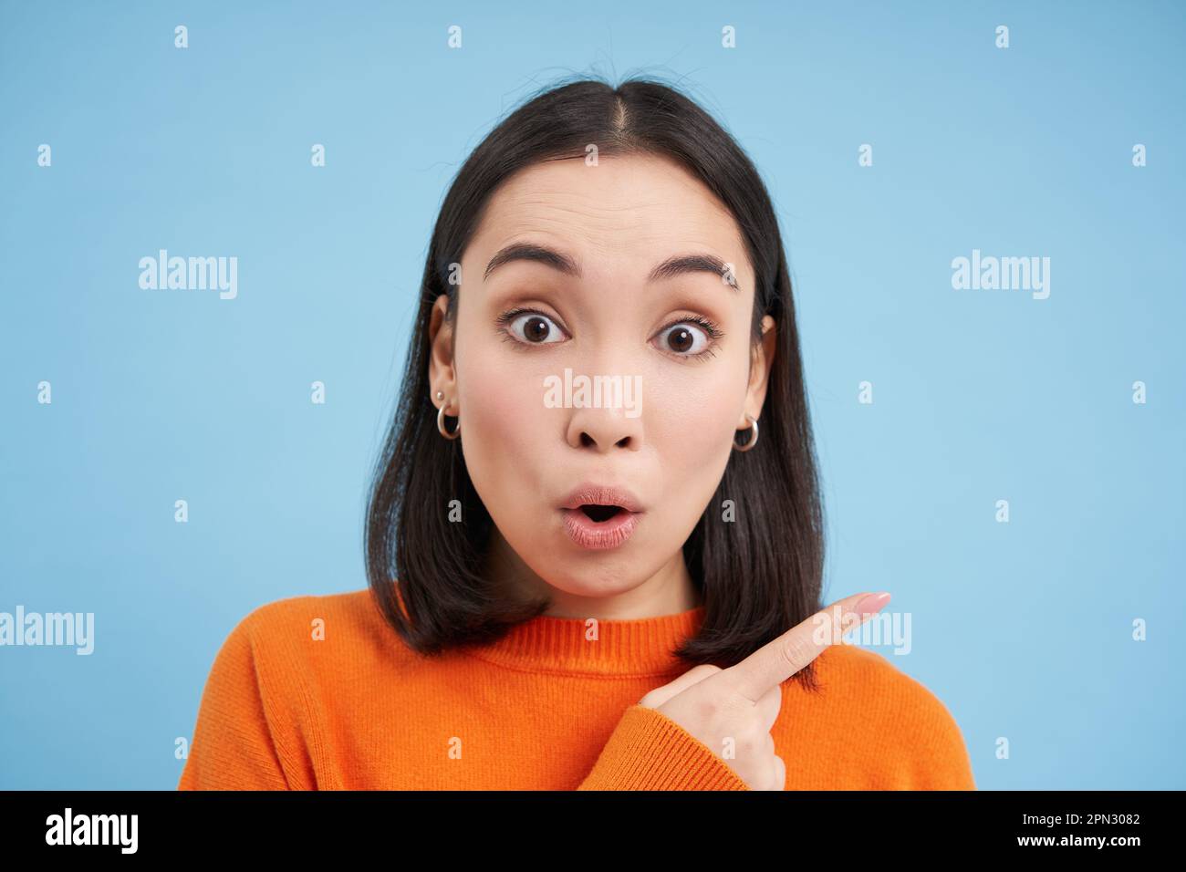 Close up of surprised asian girl, pointing finger right, showing ...