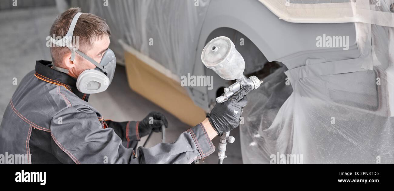 Painting the rear part of the car. Car painter wearing costume and ...
