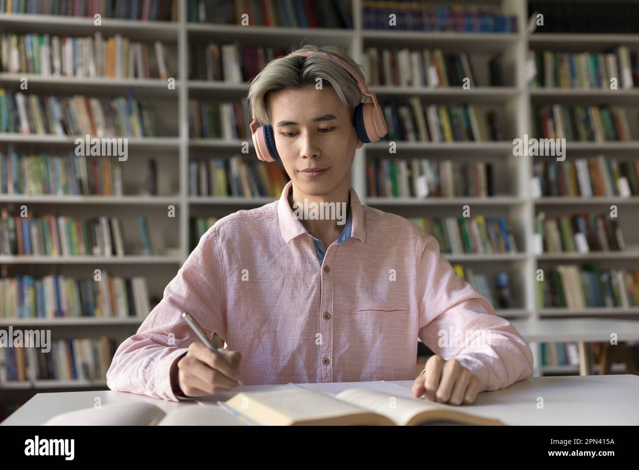 Serious focused Asian student guy in headphones studying in library ...