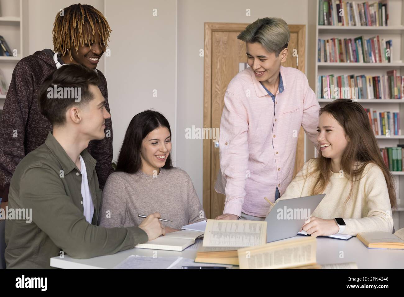 Five diverse teenage students engaged in teamwork gather in library ...