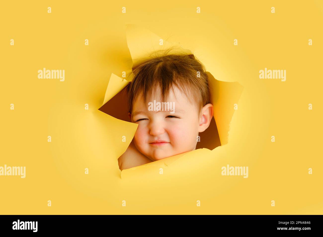 A confused baby in a hole on a paper yellow background. Torn child's ...