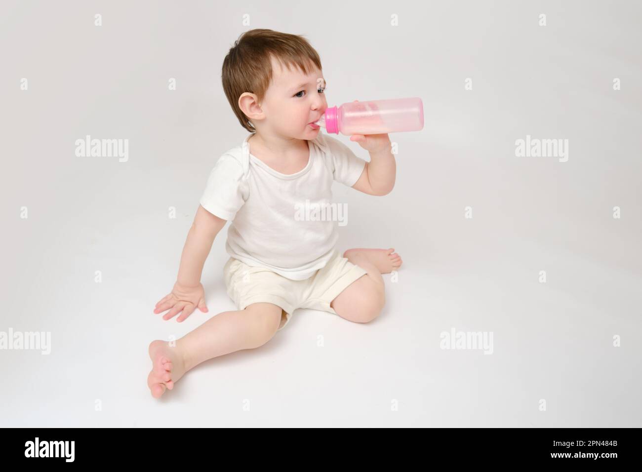 Happy baby drinks milk from bottle on studio white background. Resting ...
