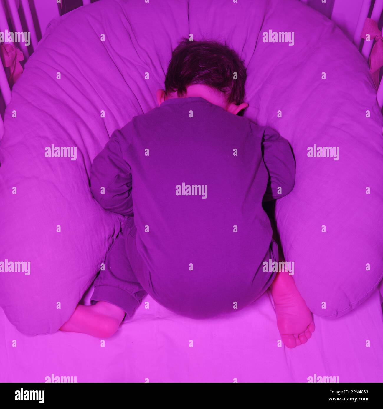 Toddler baby sleeps face down on his stomach while lying in a crib ...