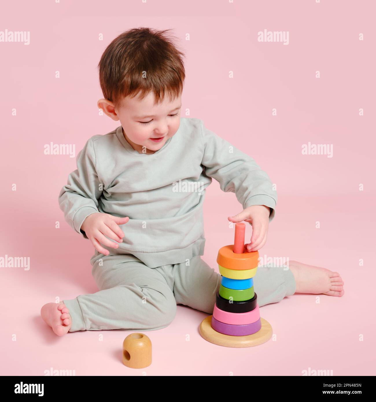 Happy toddler baby plays with a pyramid on a studio pink background ...