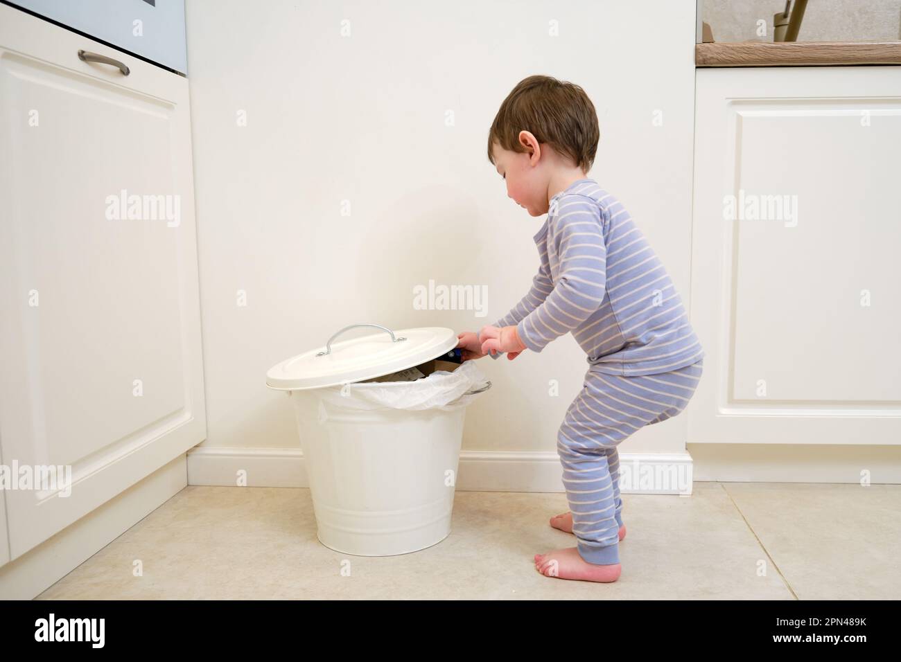 Toddler baby throws garbage in the trash can. A happy child lifts the ...