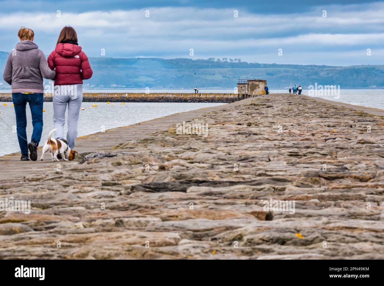 People walking along the top of long stone pier into the Firth of Forth ...