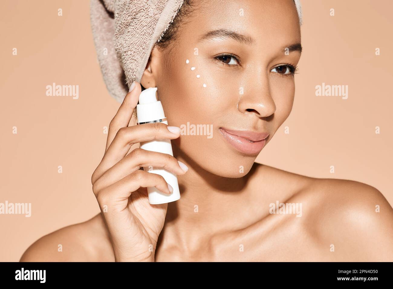 Positive curly woman applies moisturizing cream on her face, on beige ...