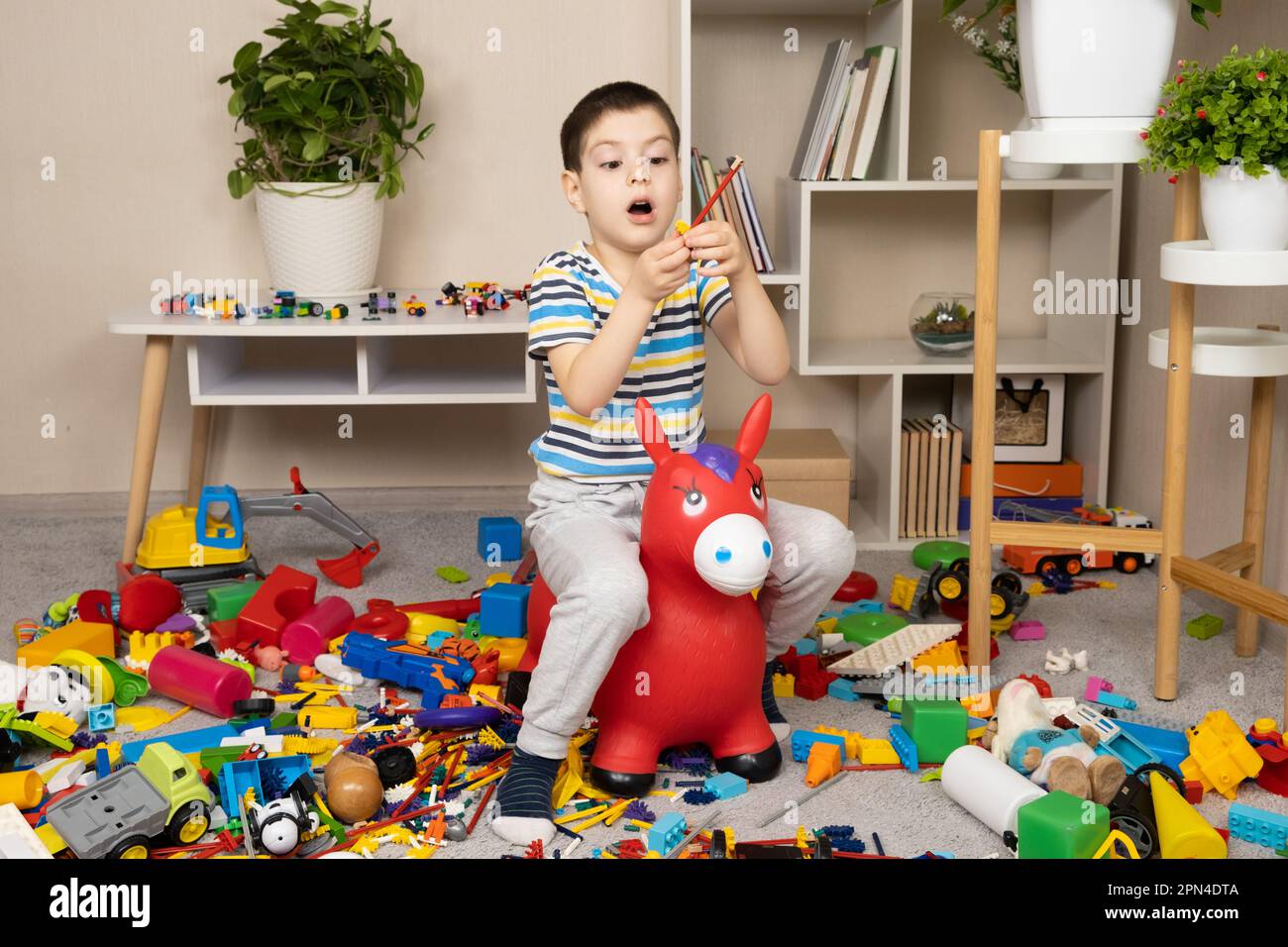 A little boy is jumping on an inflatable rubber donkey among the mess ...