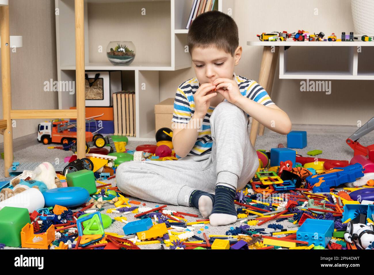 Little boy playing with toys sitting on the floor among scattered toys ...