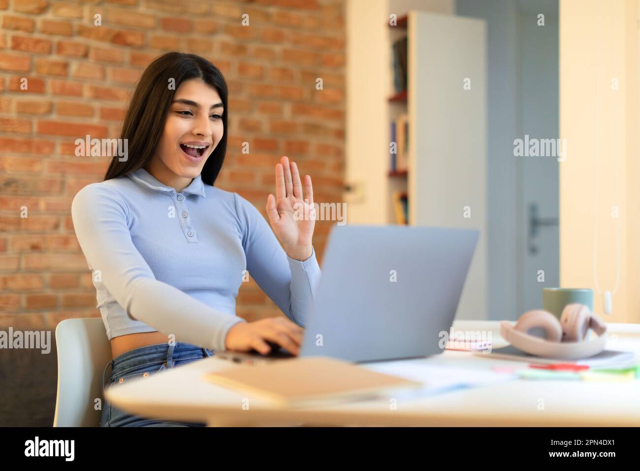 Excited spanish lady having video call on laptop, waving hand, saying ...