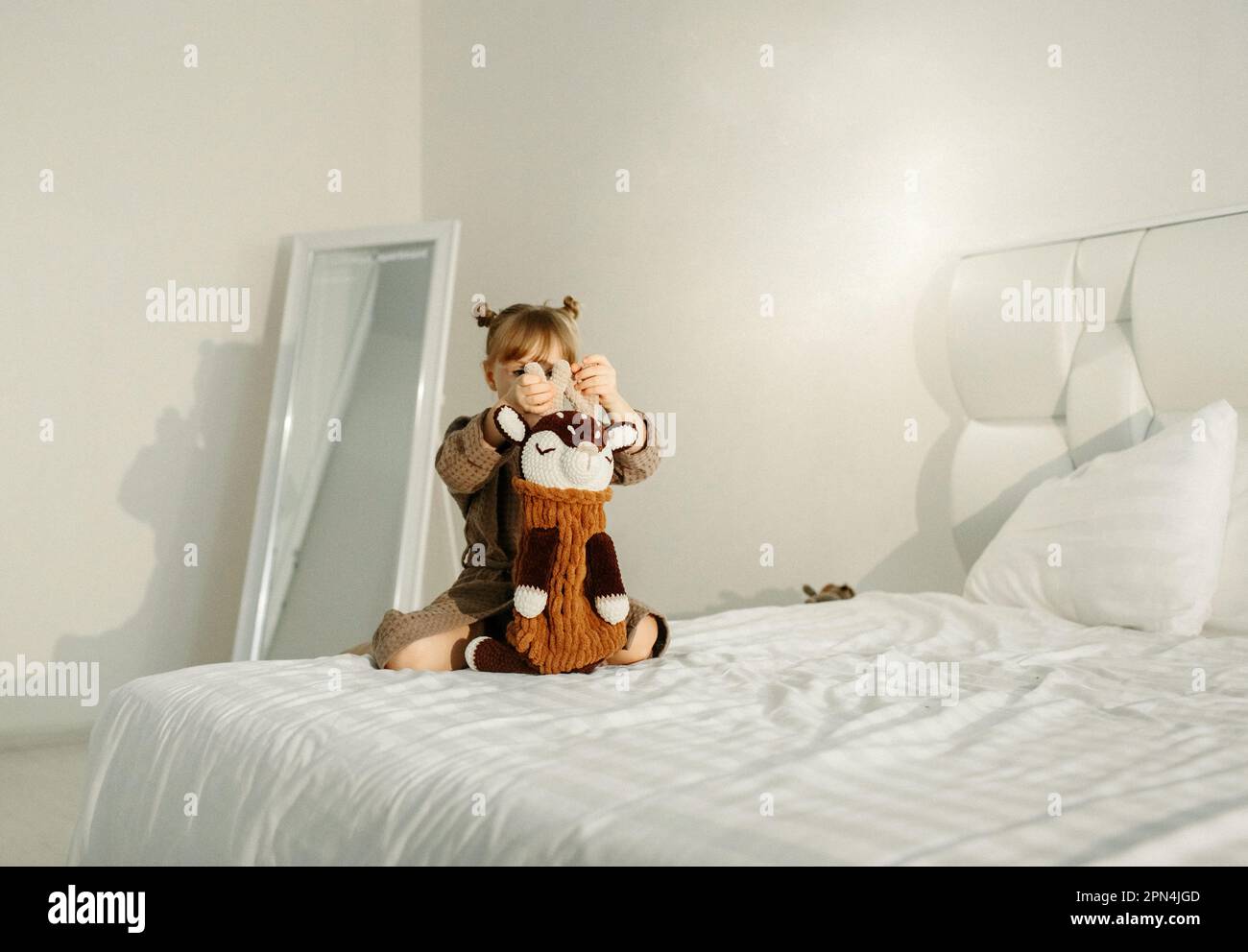 A girl in a dressing gown plays in bed with knitted toys Stock Photo ...