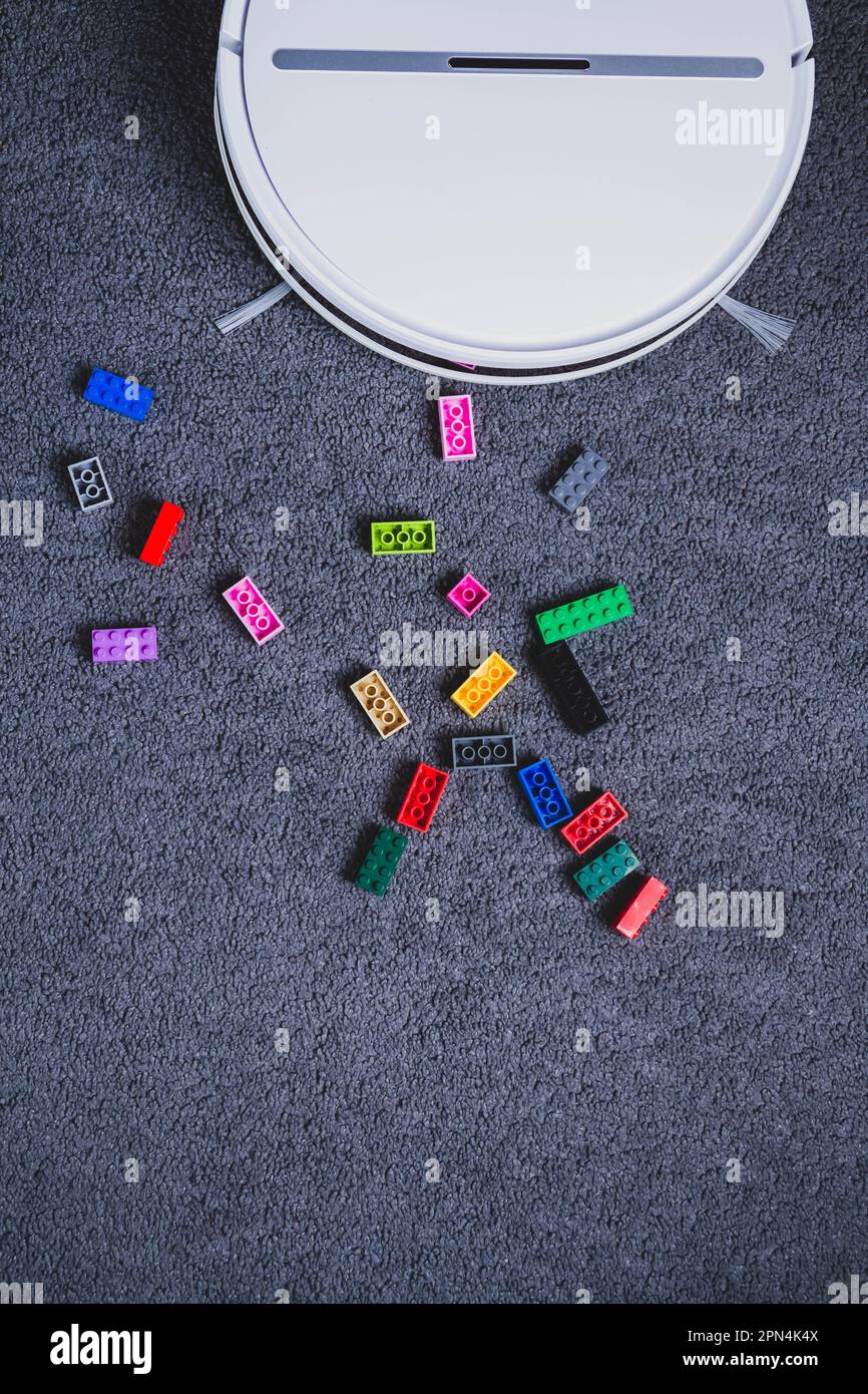 A robot vacuum cleaner cleans children's toys on the floor. Carpet and ...