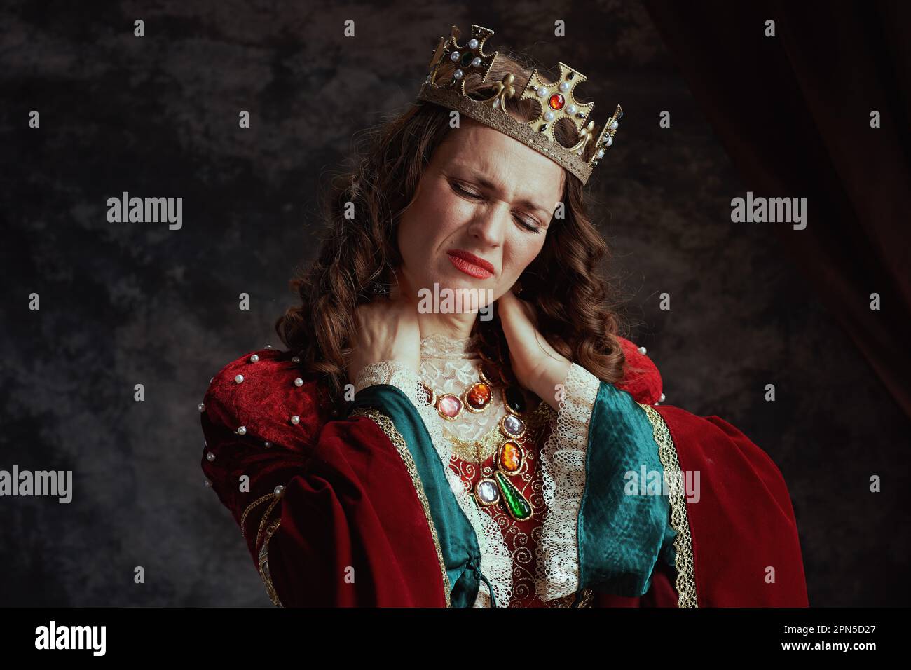 stressed medieval queen in red dress with crown having neck pain on ...