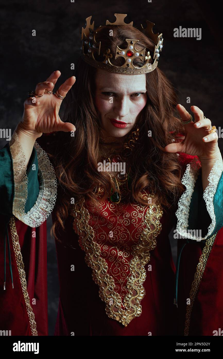 scary medieval queen in red dress with white makeup and crown on dark ...
