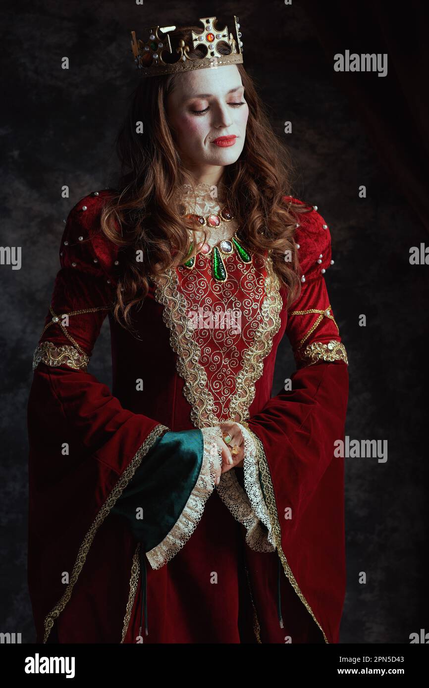 medieval queen in red dress with white makeup and crown on dark gray ...