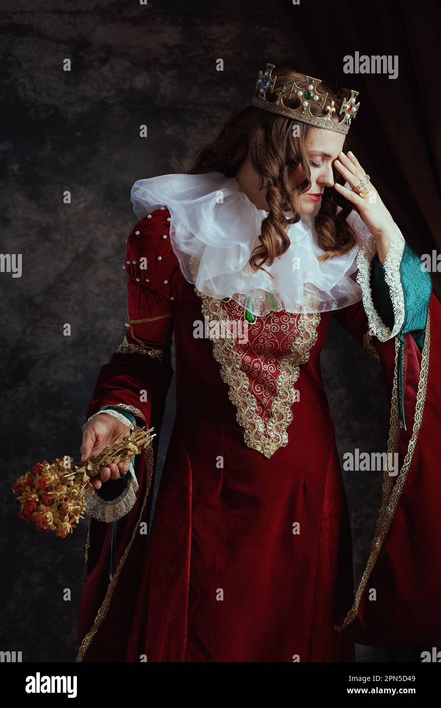 unhappy medieval queen in red dress with dried flower, white collar and ...